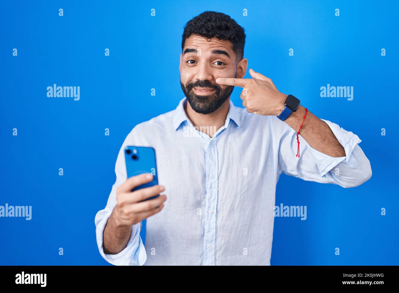 Hispanic man with beard using smartphone typing message pointing with ...