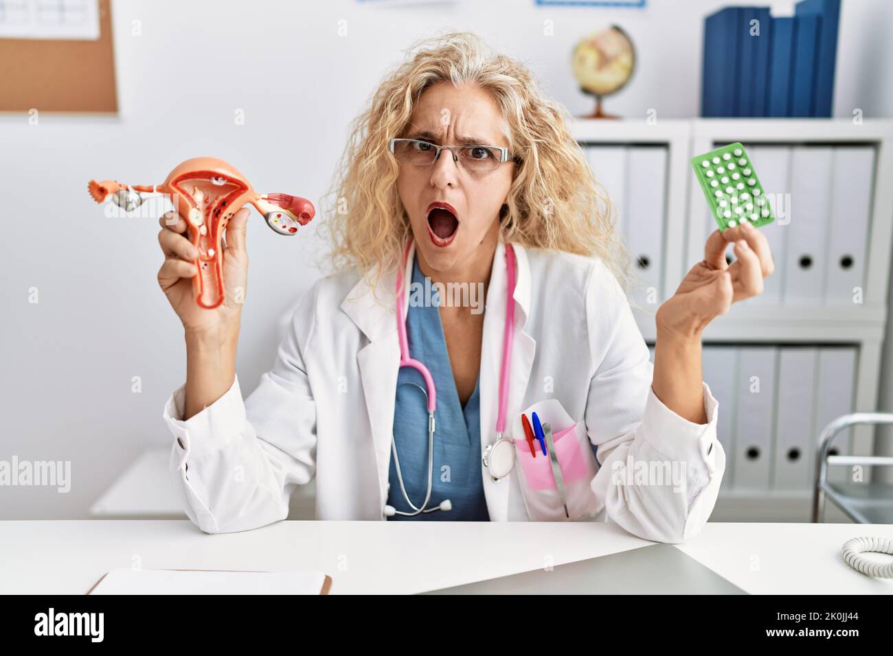 Middle age doctor woman holding birth control pills in shock face ...