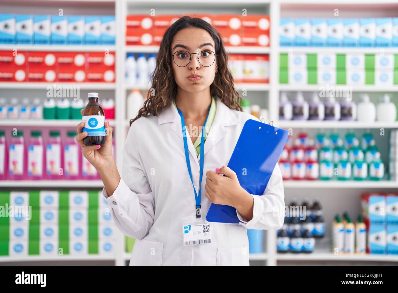 Young hispanic woman working at pharmacy drugstore holding syrup ...