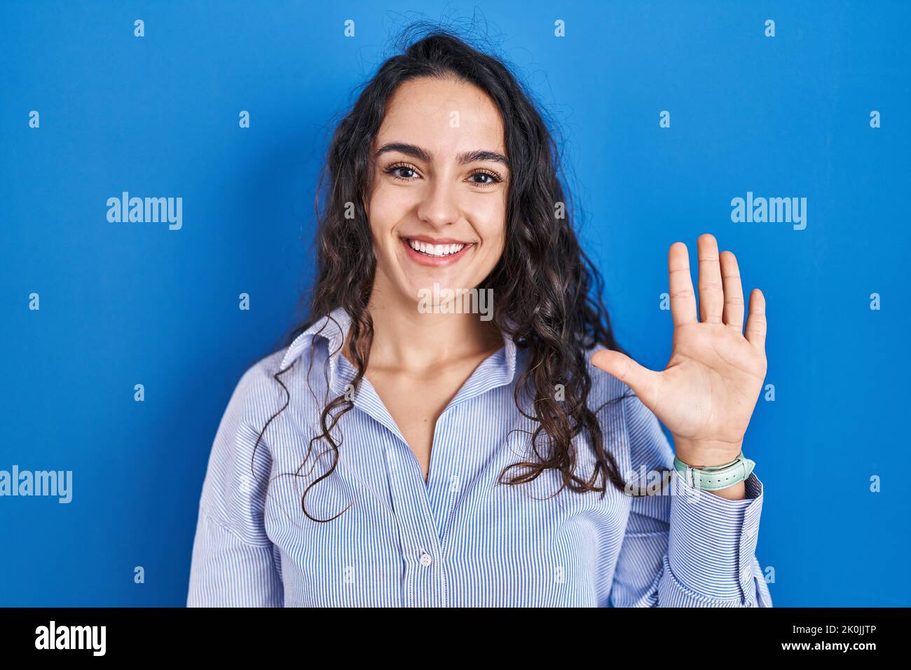 Young brunette woman standing over blue background showing and pointing ...