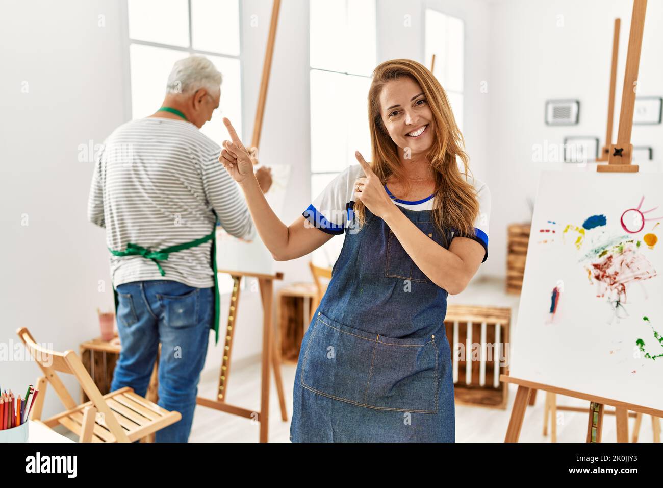 Hispanic woman wearing apron at art studio smiling and looking at the ...