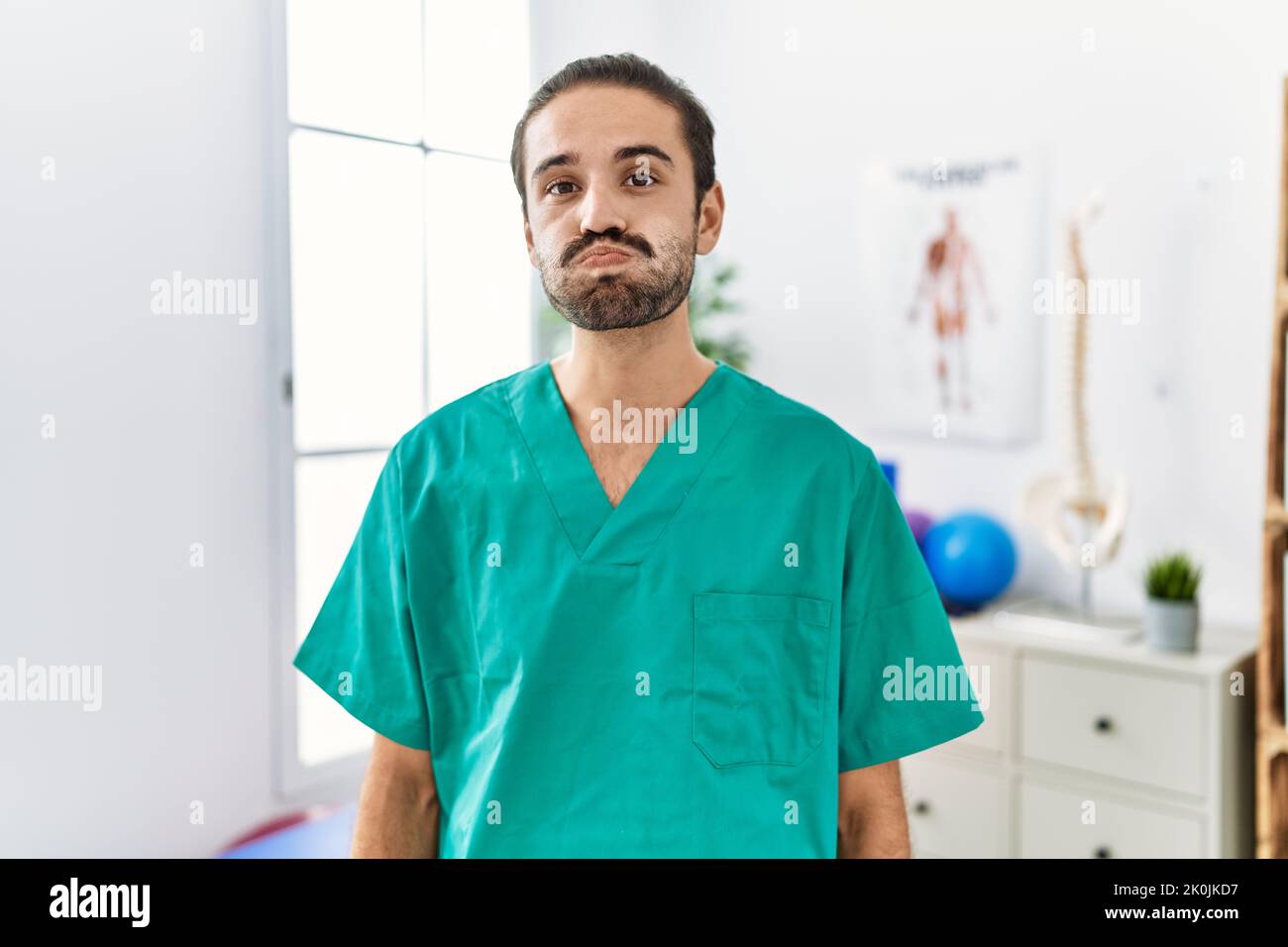 Young physiotherapist working at pain recovery clinic puffing cheeks ...