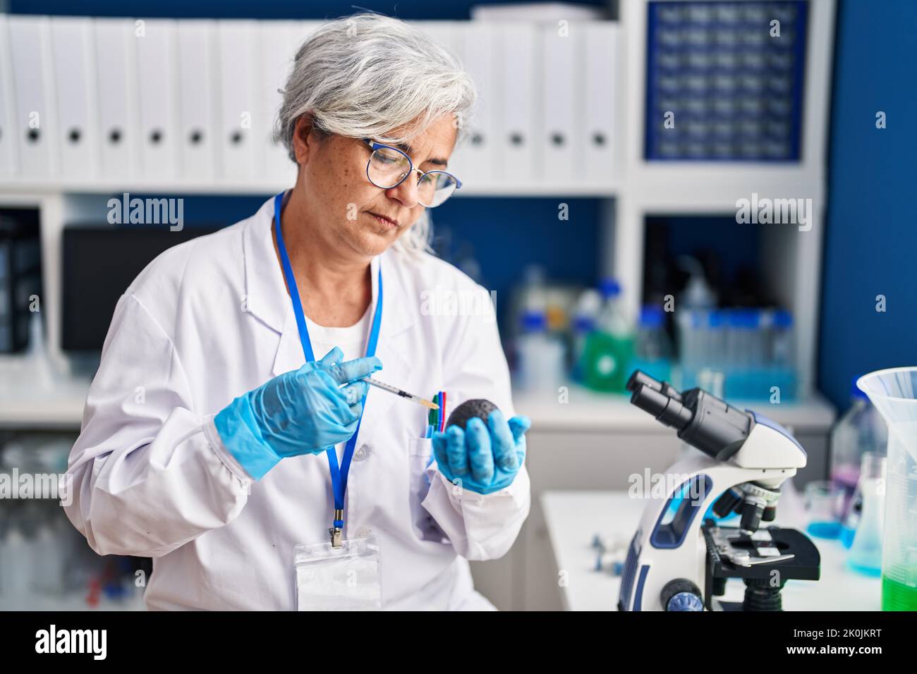 Middle age woman wearing scientist uniform analysing avocado at ...
