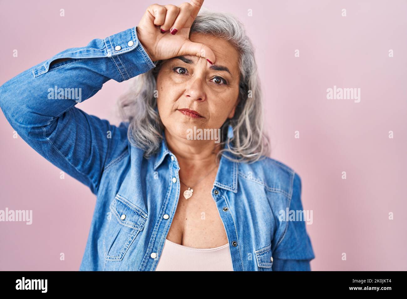 Middle age woman with grey hair standing over pink background making ...
