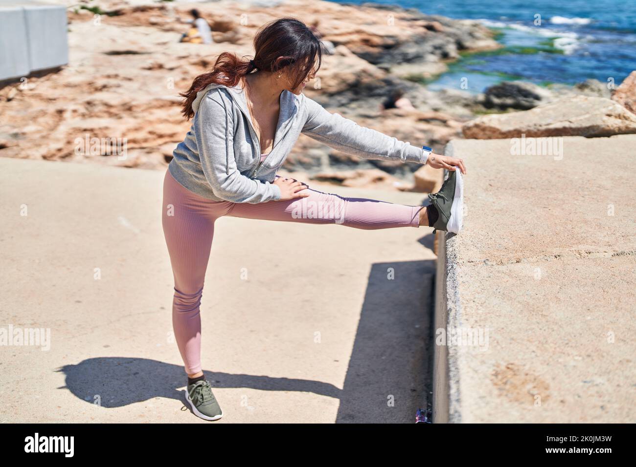 Young hispanic woman stretching legs training at seaside Stock Photo ...