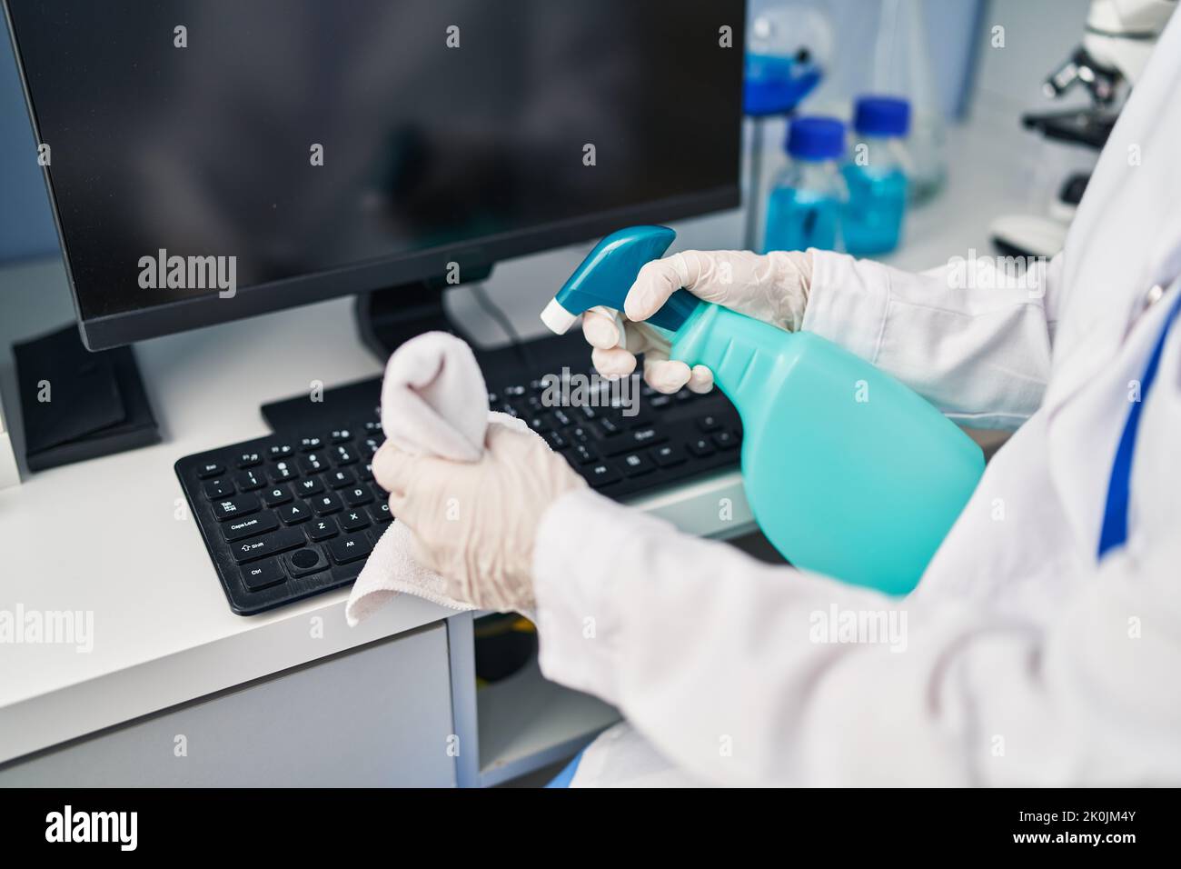 Young hispanic woman wearing scientist uniform cleaning using sanitizer ...