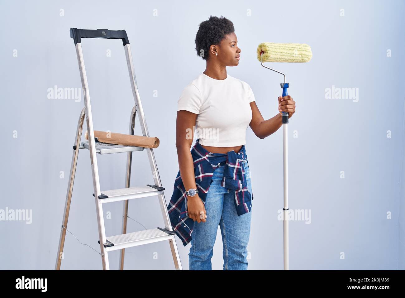 African american woman holding roller painter looking to side, relax ...