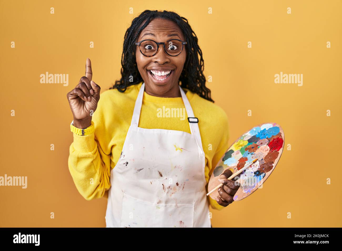 African woman holding painter palette pointing finger up with ...