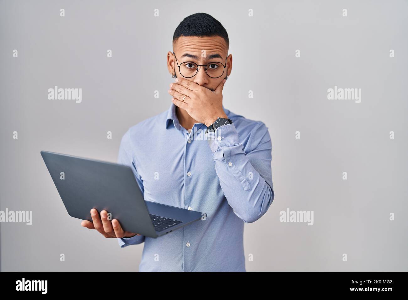 Young hispanic man working using computer laptop shocked covering mouth ...