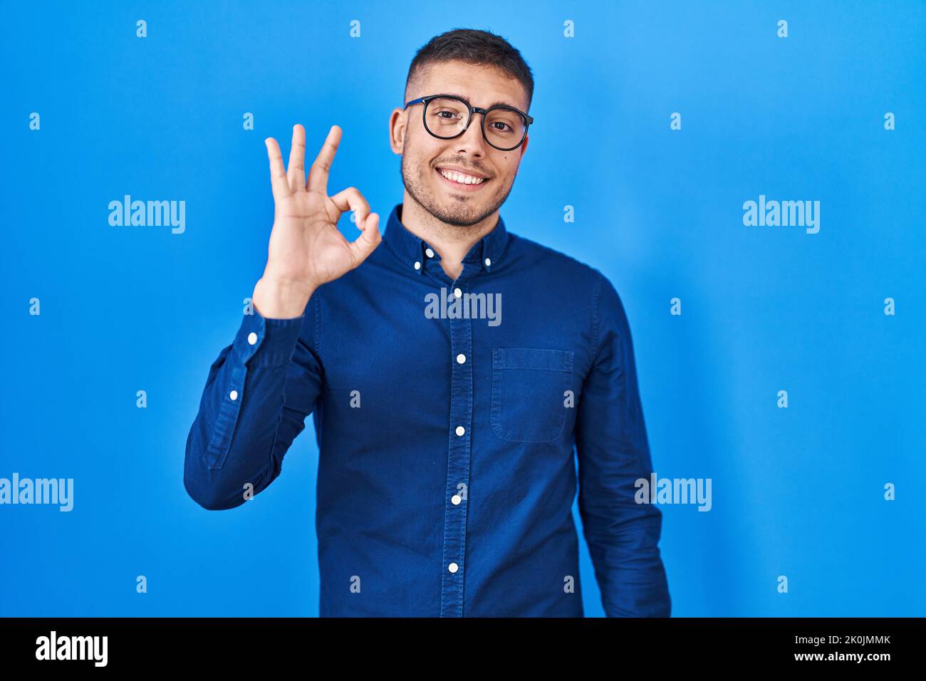 Young hispanic man wearing glasses over blue background smiling ...