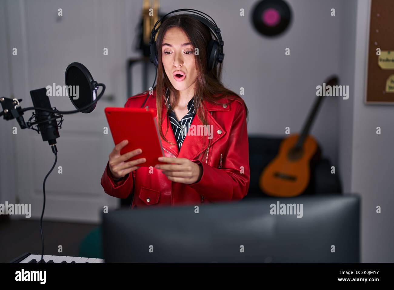 Young brunette woman singing song using microphone scared and amazed ...