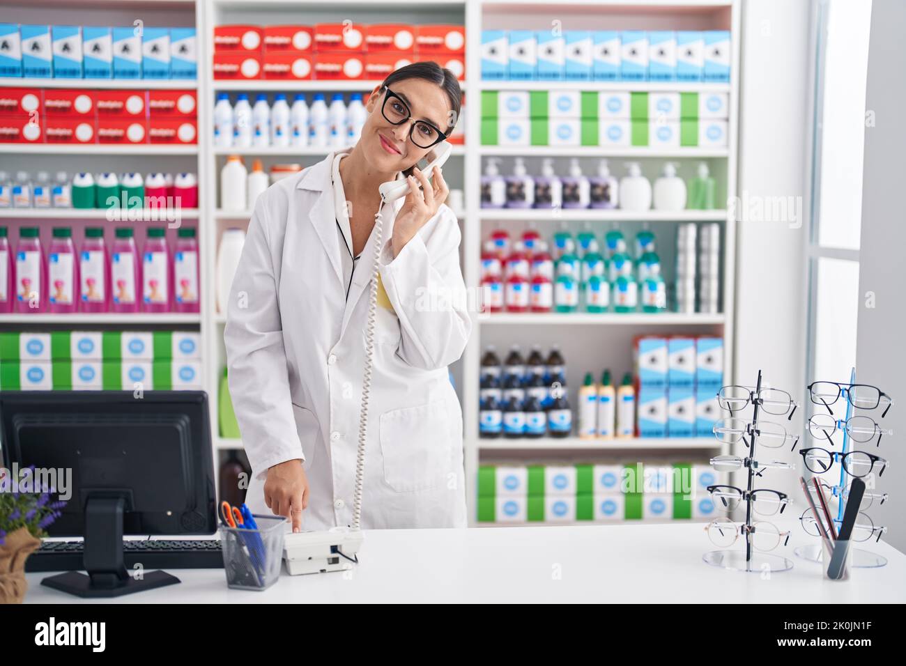 Young beautiful hispanic woman pharmacist talking on telephone using ...