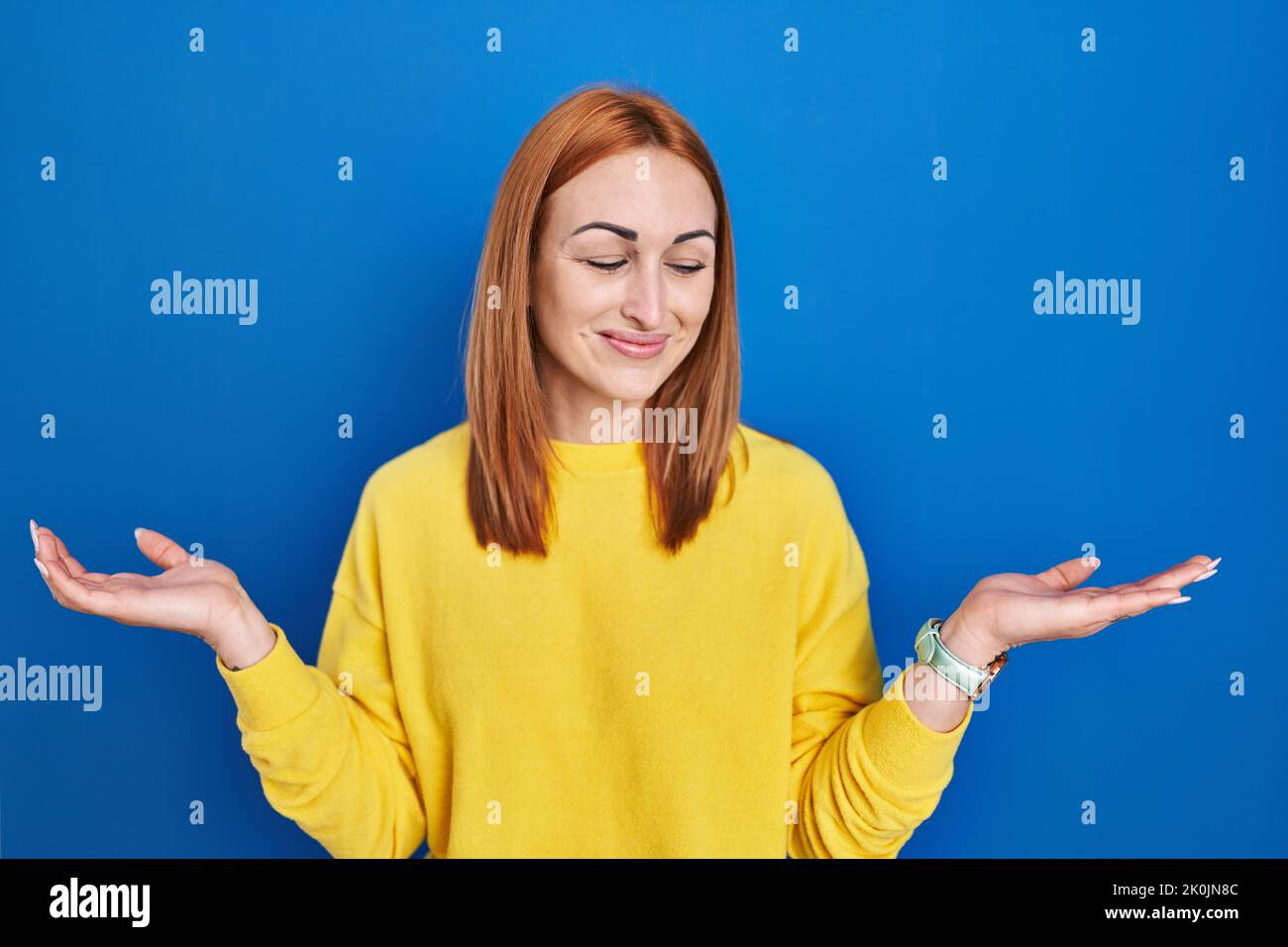 Young woman standing over blue background smiling showing both hands ...