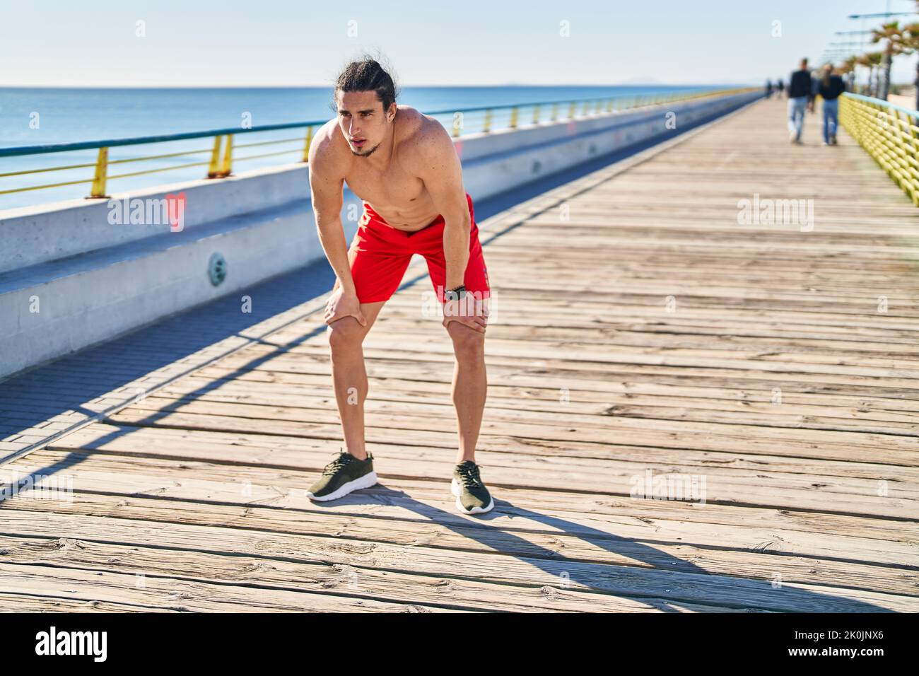 Young man resting with hands on knee at seaside Stock Photo - Alamy