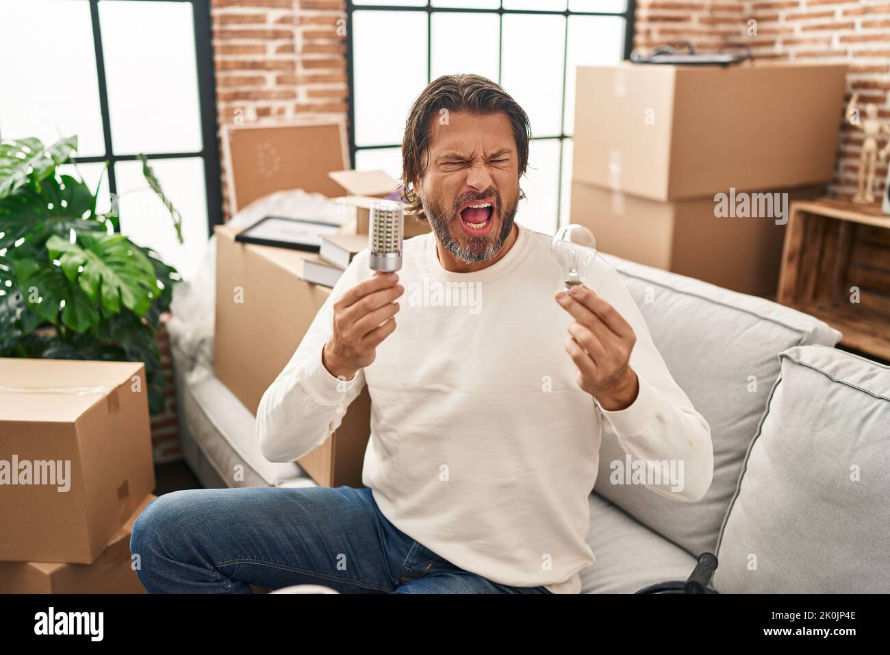 Handsome middle age man holding led lightbulb and incandescent bulb ...