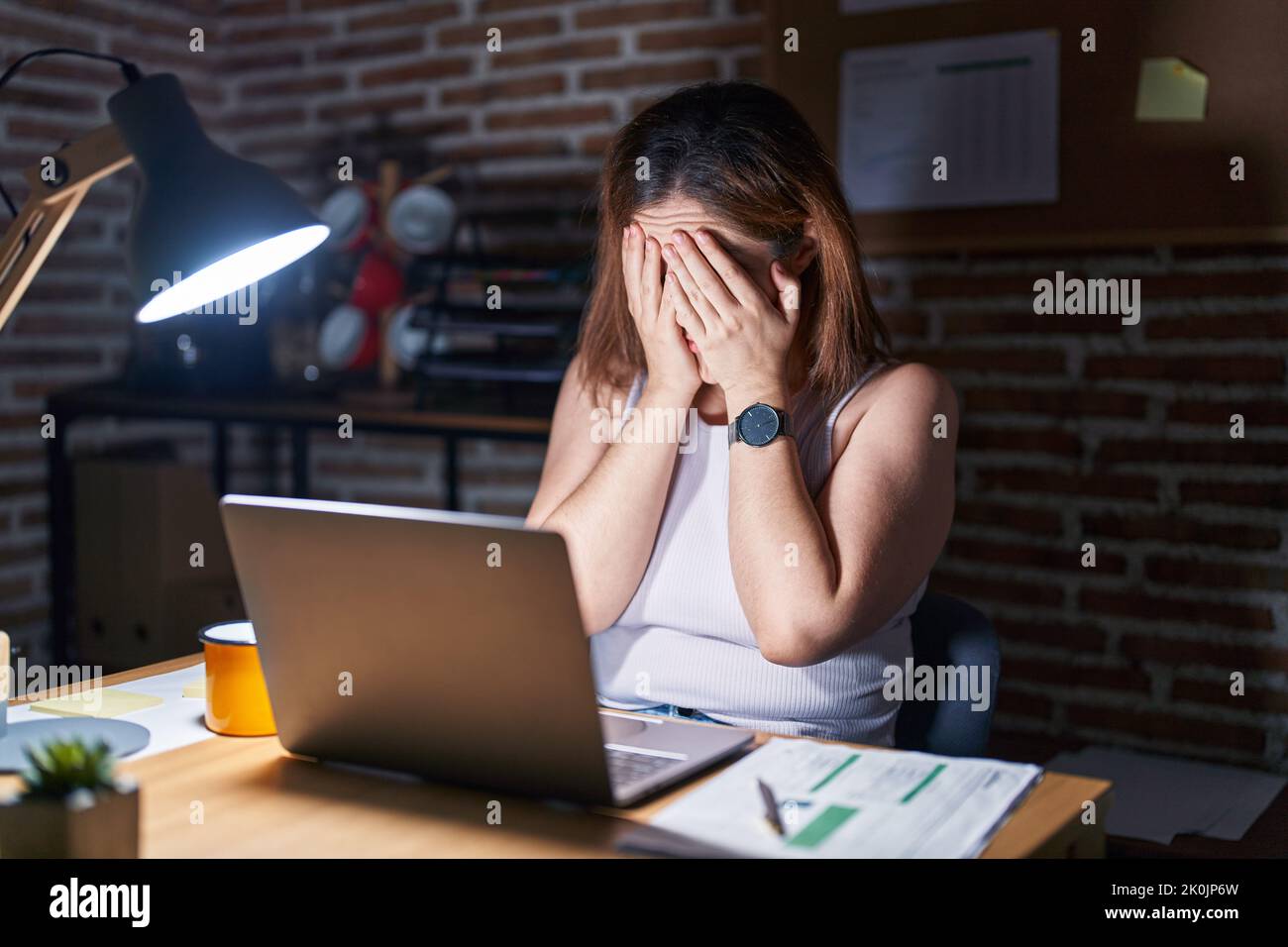 Brunette woman working at the office at night with sad expression ...