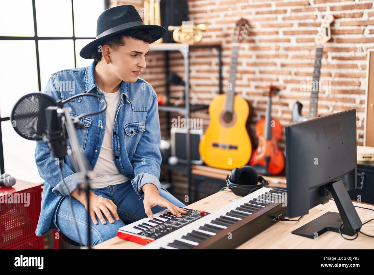 Young non binary man musician playing piano keyboard at music studio ...