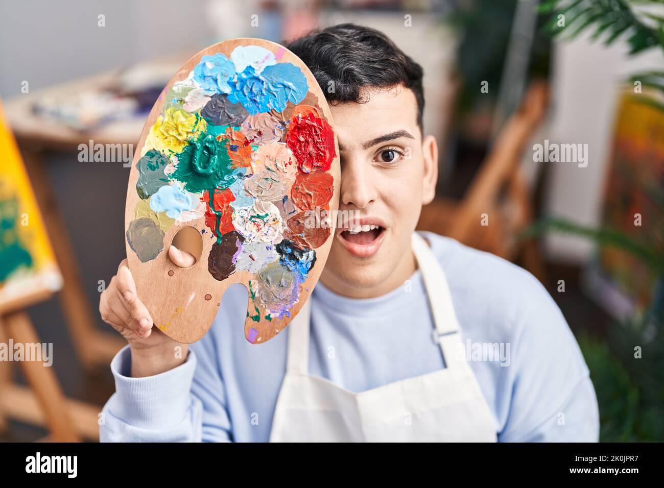 Non binary person holding palette close to face scared and amazed with ...