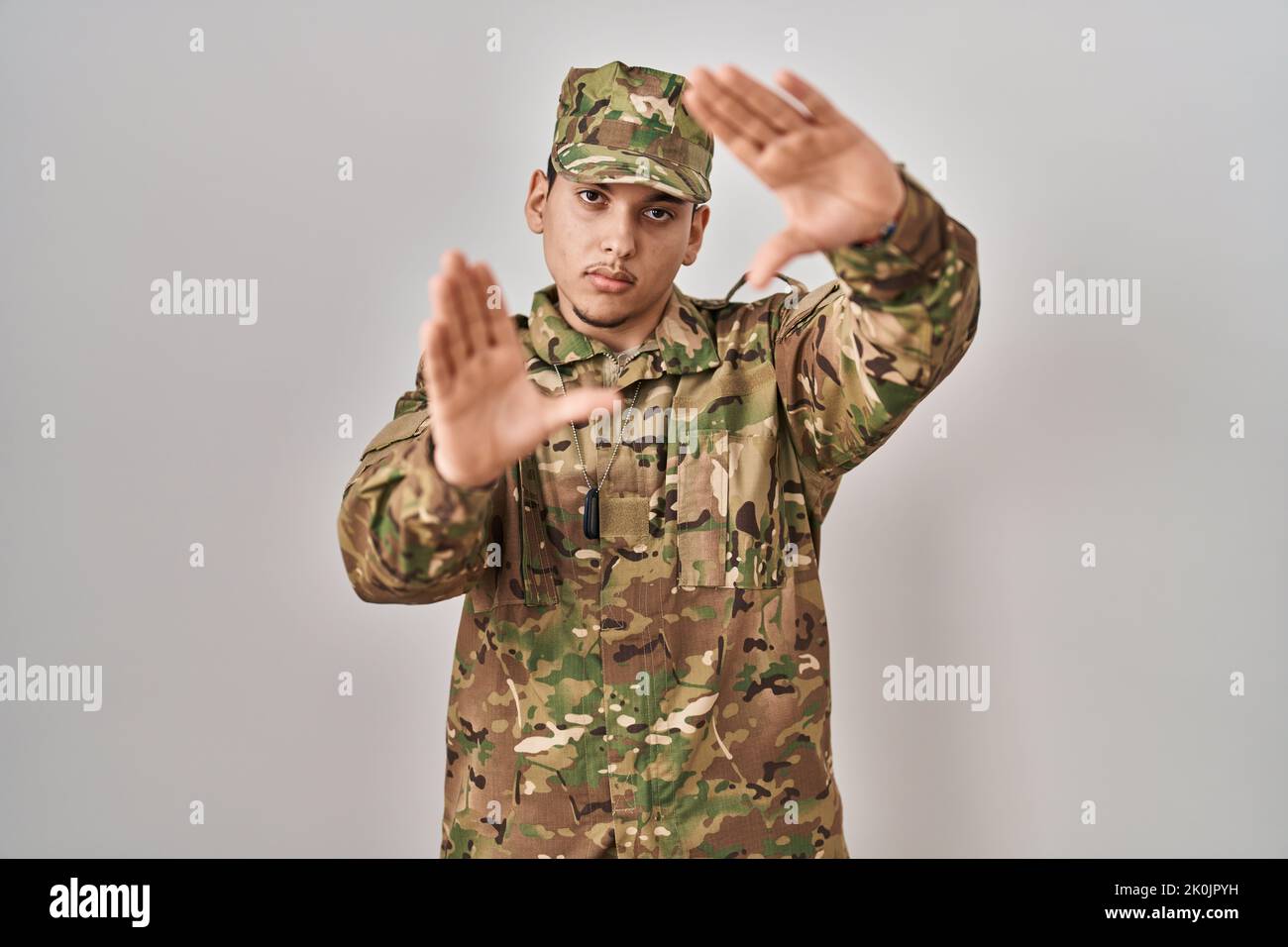 Young arab man wearing camouflage army uniform doing frame using hands ...