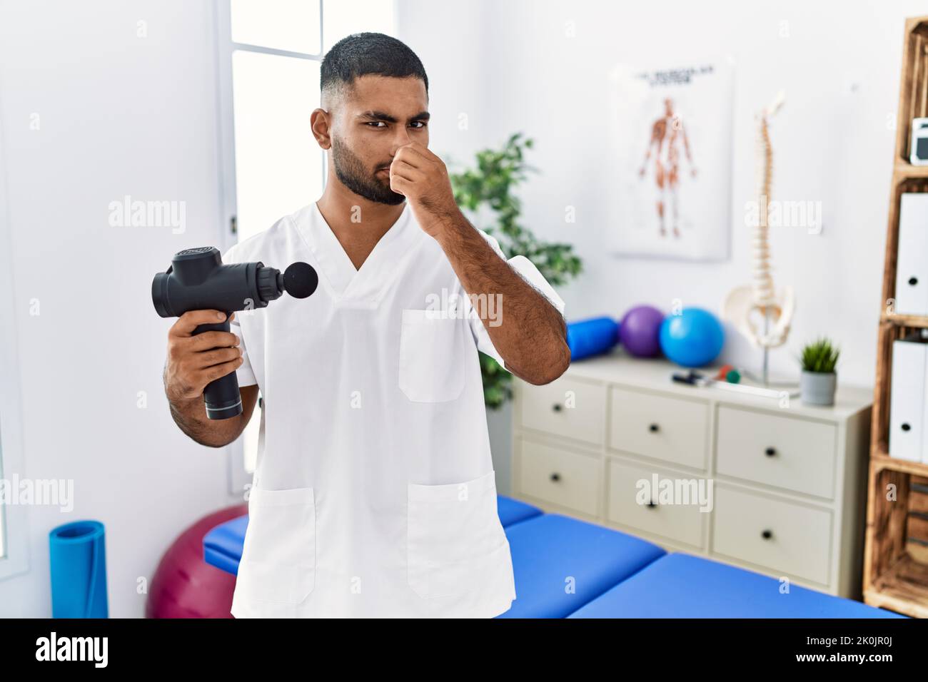 Young indian physiotherapist holding therapy massage gun at wellness ...