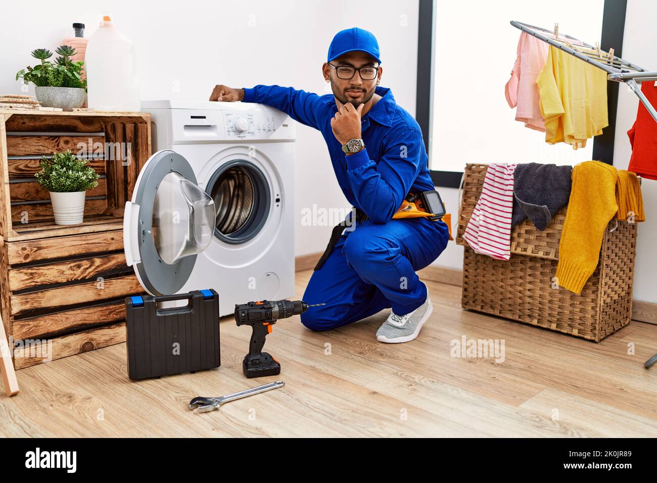 Young indian technician working on washing machine looking confident at ...