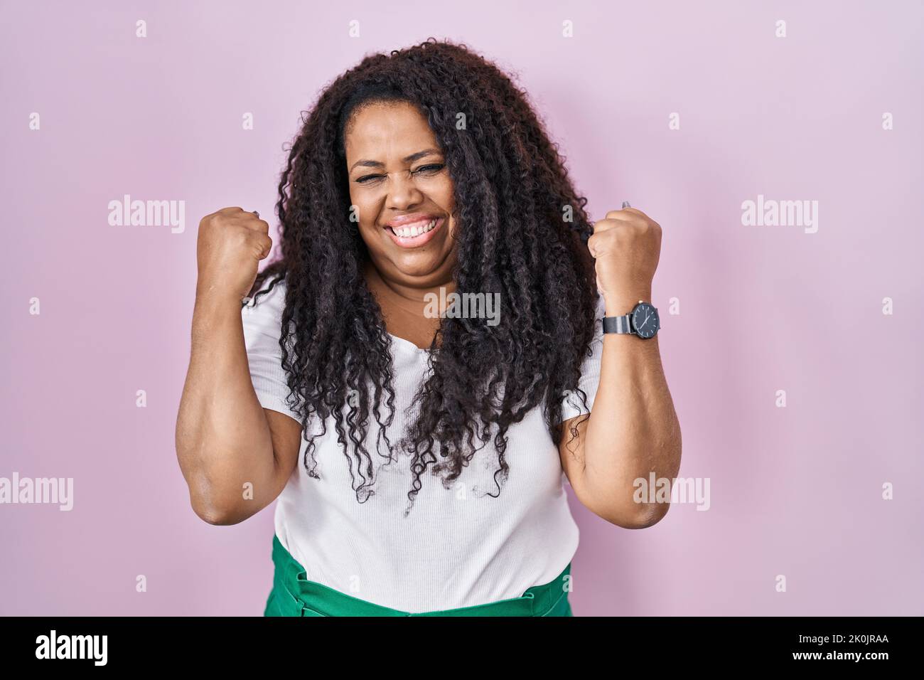Plus size hispanic woman standing over pink background celebrating ...