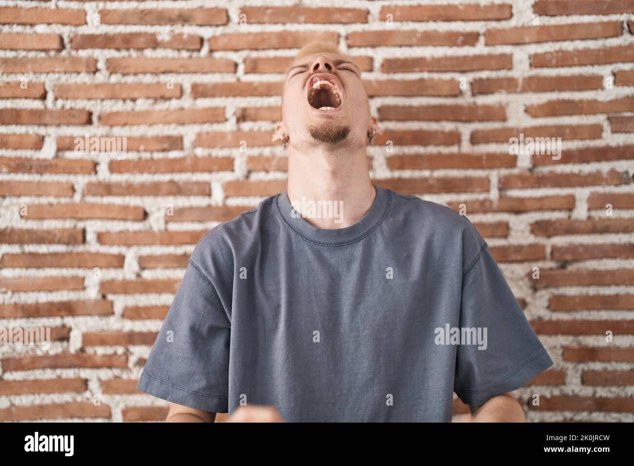 Young caucasian man standing over bricks wall angry and mad screaming ...
