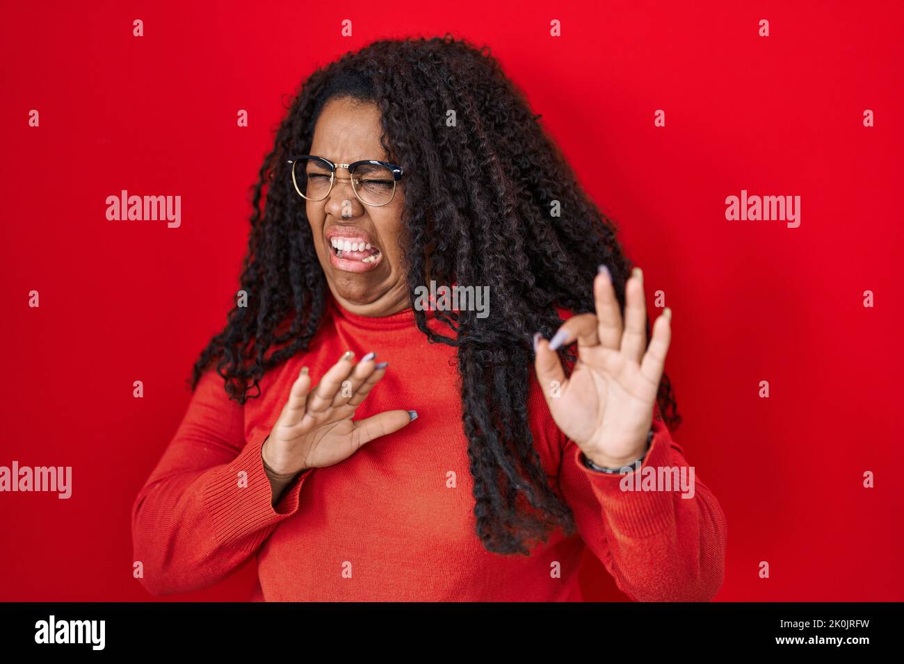 Plus size hispanic woman standing over red background disgusted ...
