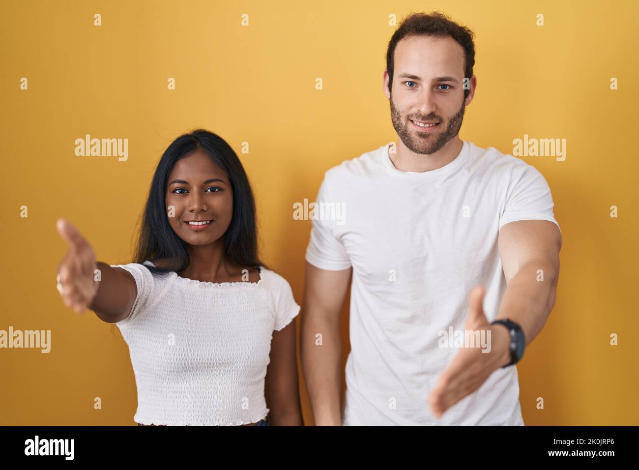 Interracial couple standing over yellow background smiling friendly ...