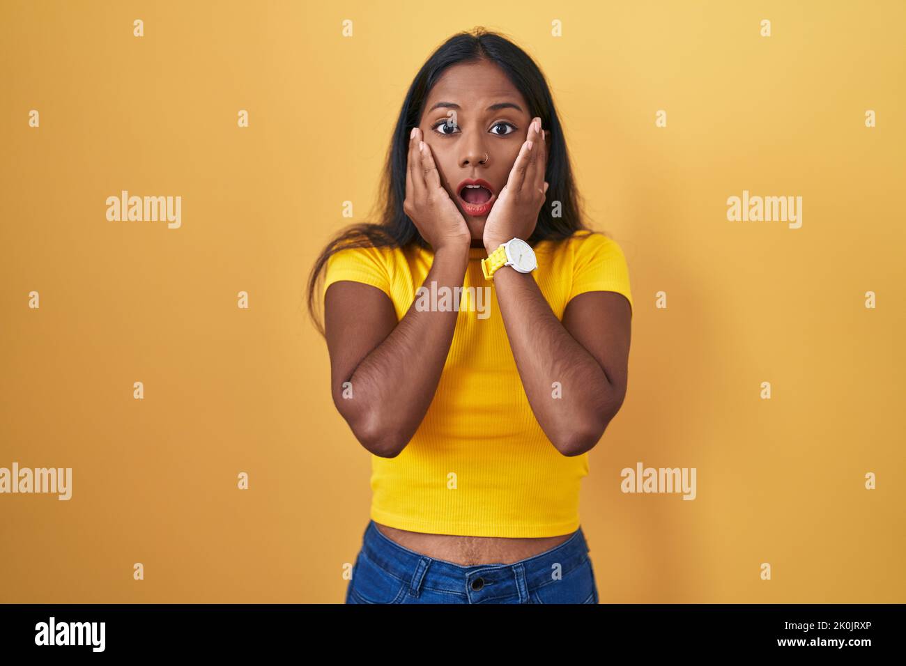 Young indian woman standing over yellow background afraid and shocked ...