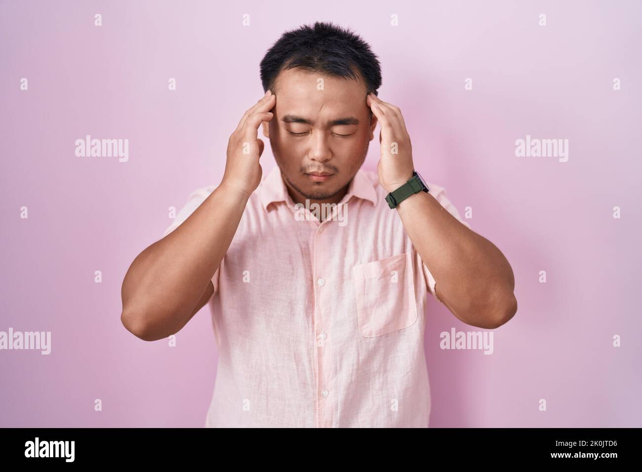 Chinese young man standing over pink background with hand on head ...