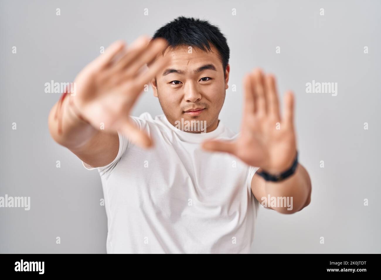 Young chinese man standing over white background doing frame using ...