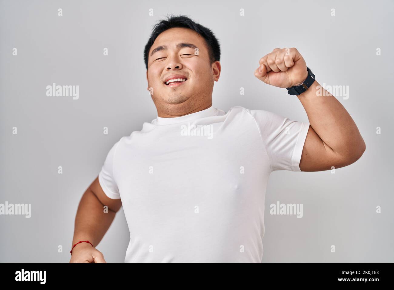 Young chinese man standing over white background stretching back, tired ...