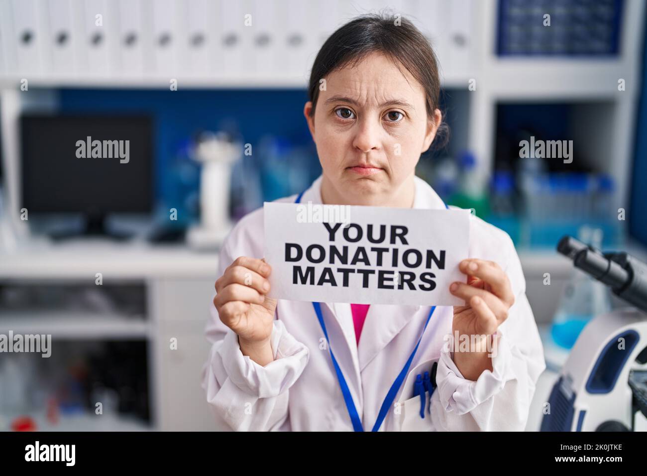 Woman with down syndrome working at scientist laboratory holding your donation matters banner ...