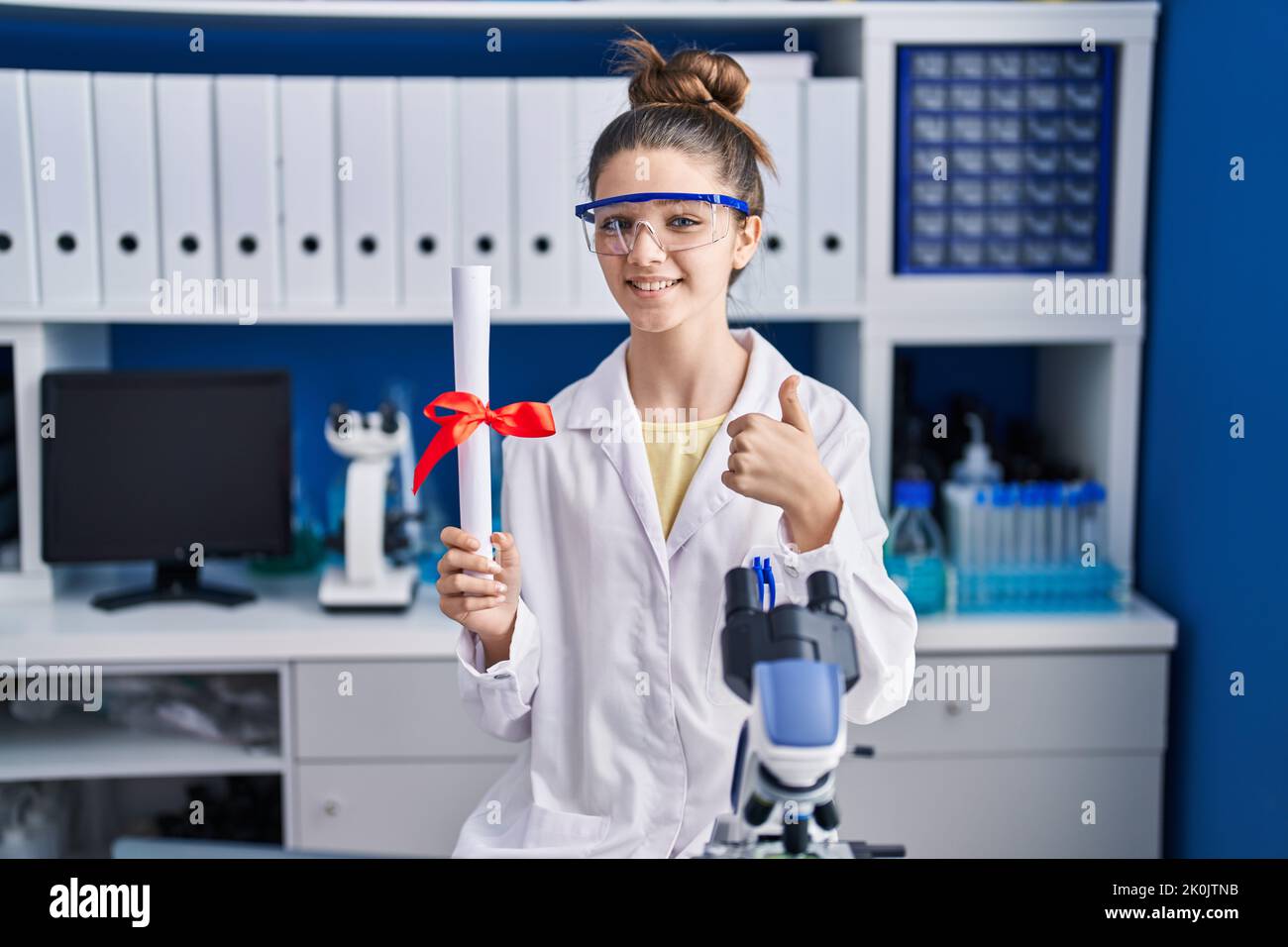Teenager girl working at scientist laboratory holding degree smiling ...