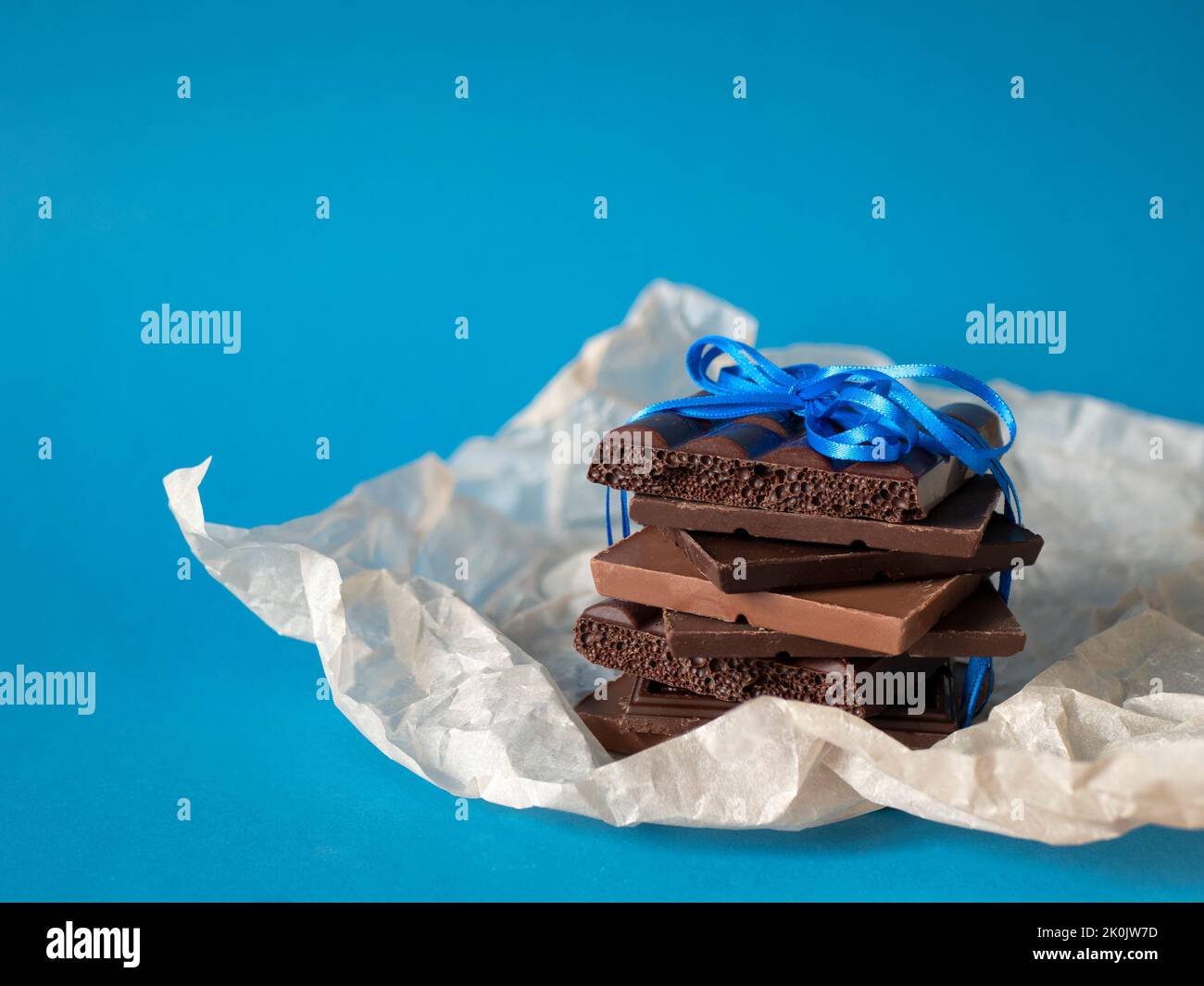 Stack of assorted chocolate pieces tied with a blue ribbon on blue ...