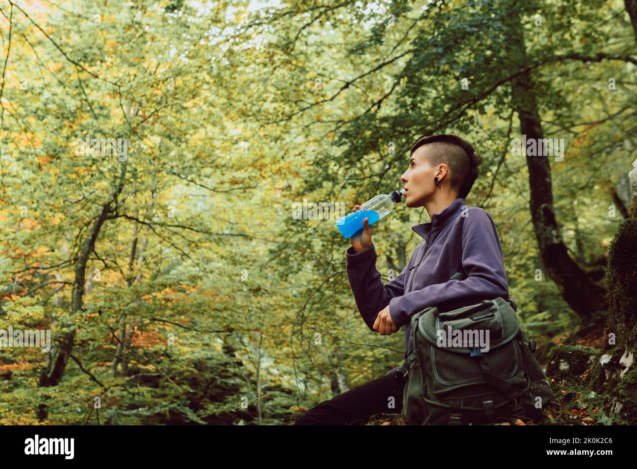 Side view of young lady with mohawk hairstyle having bottle of fresh ...