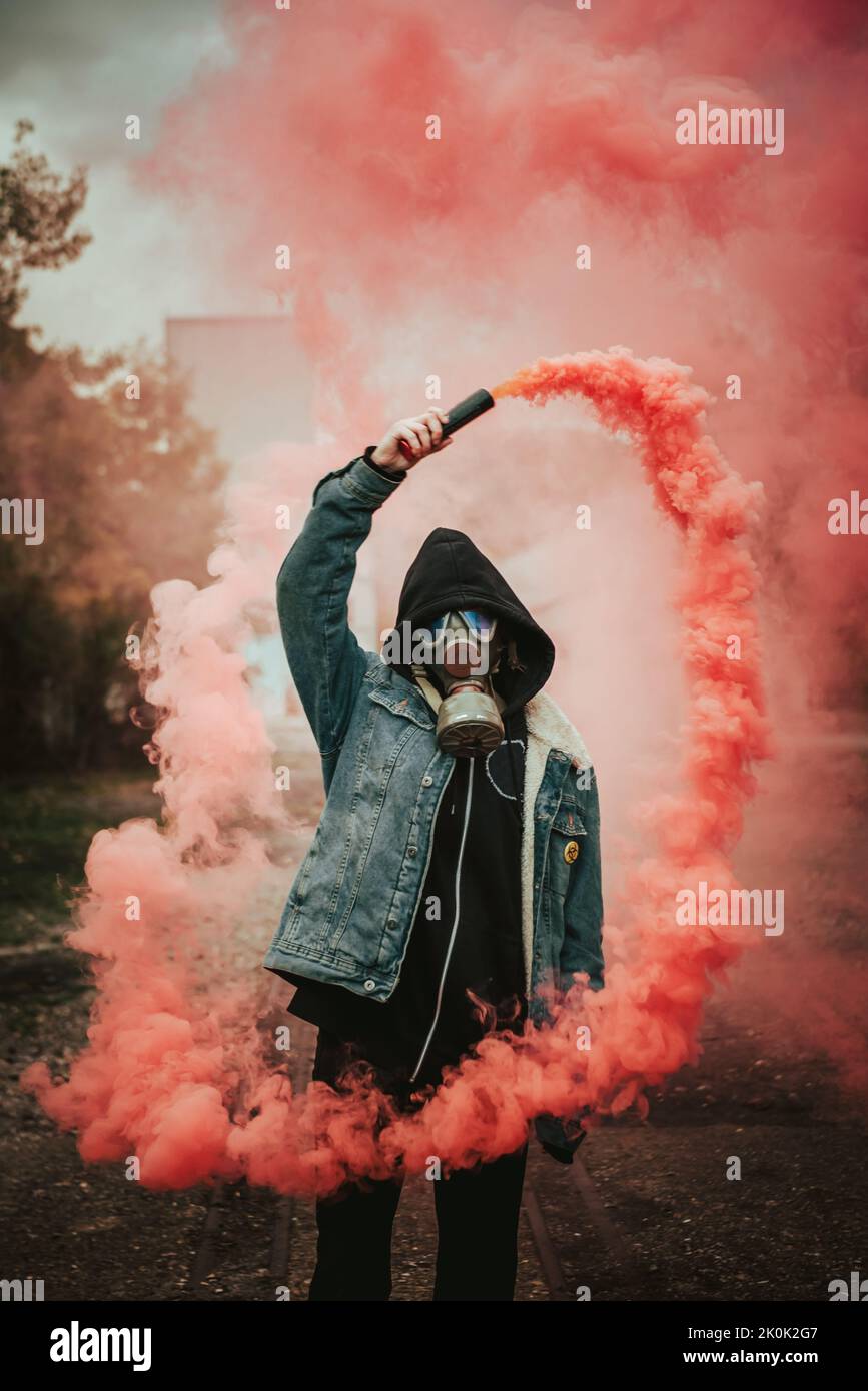 Person in gas mask and hood keeping bomb with pink fume in raised hand ...