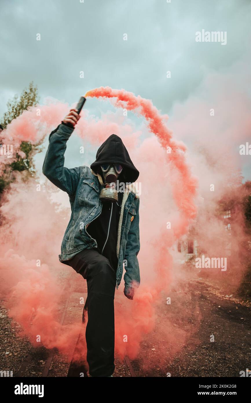 Person in gas mask and hood keeping bomb with pink fume in raised hand ...