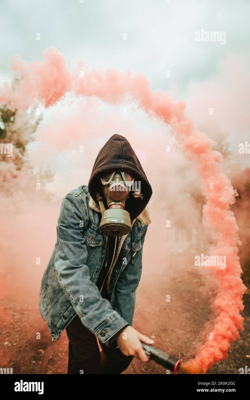 Person in gas mask and hood keeping bomb with pink fume in raised hand ...