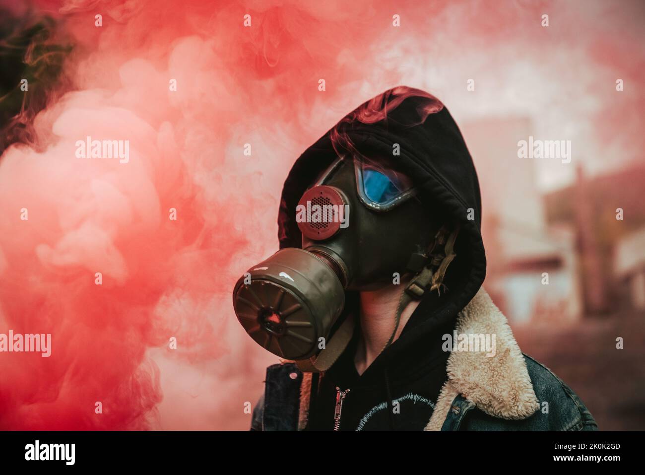 Person in gas mask and hood keeping bomb with pink fume in raised hand ...