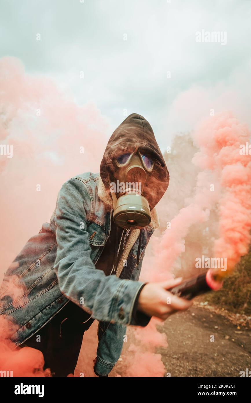 Person in gas mask and hood keeping bomb with pink fume in raised hand ...