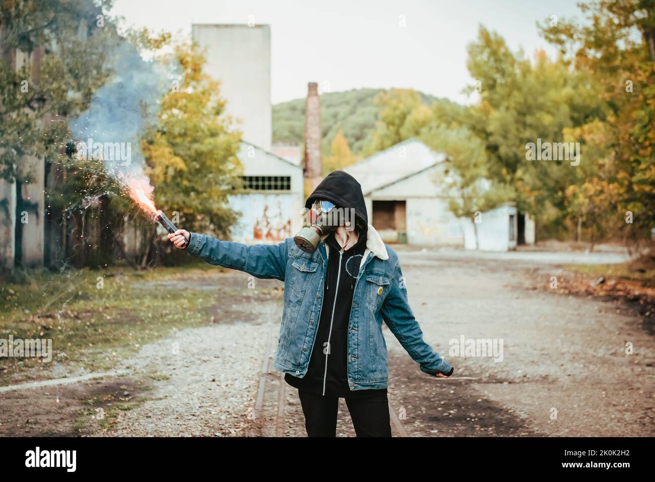 Person in gas mask and hood keeping bomb with pink fume in raised hand ...
