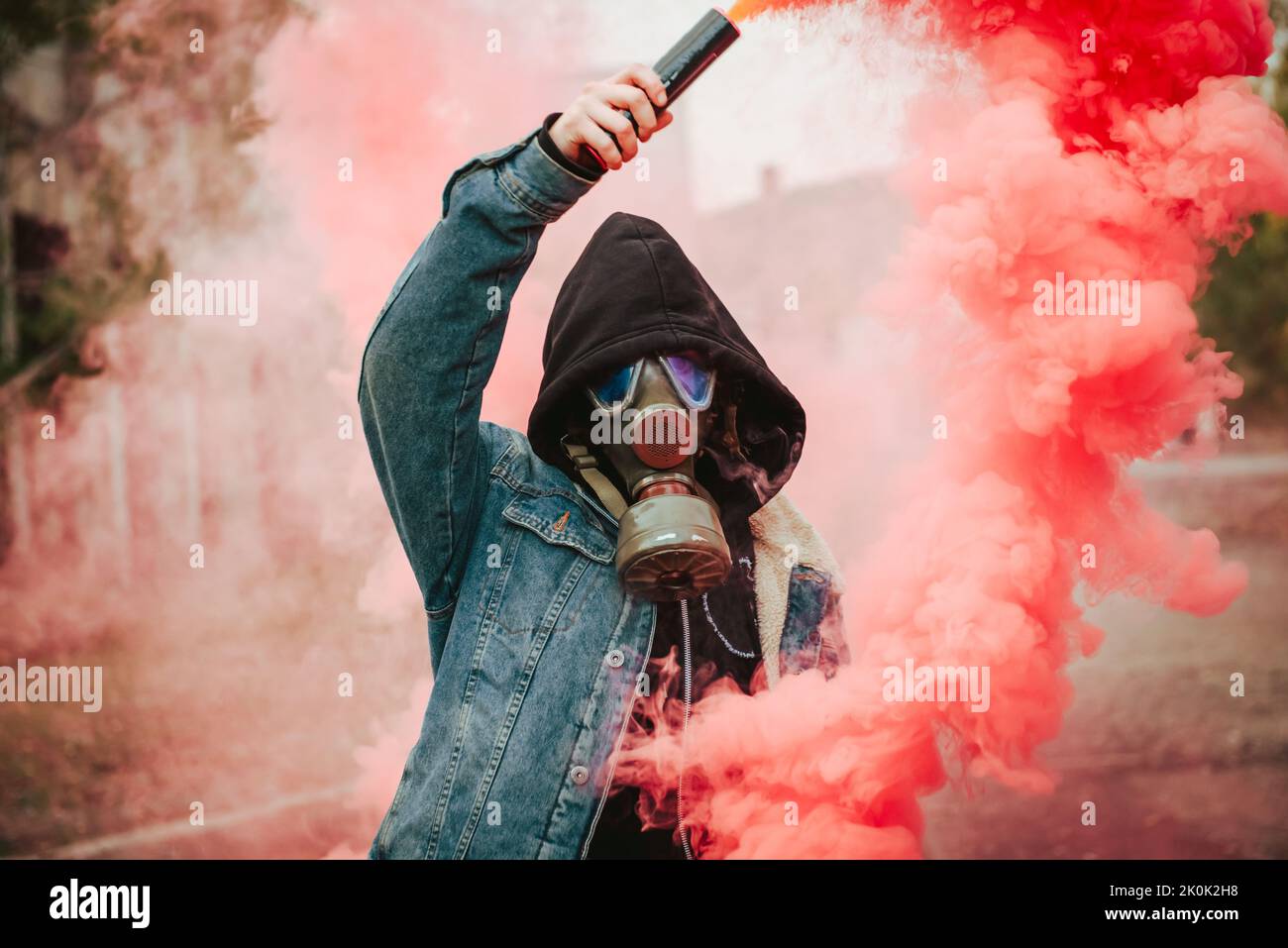 Person in gas mask and hood keeping bomb with pink fume in raised hand ...