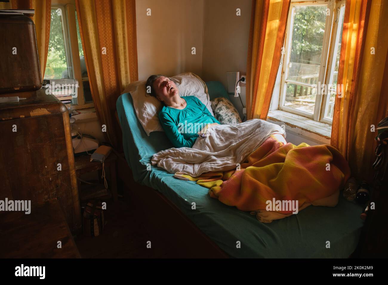 Senior woman with paralysis lying under blanket on medical bed near ...