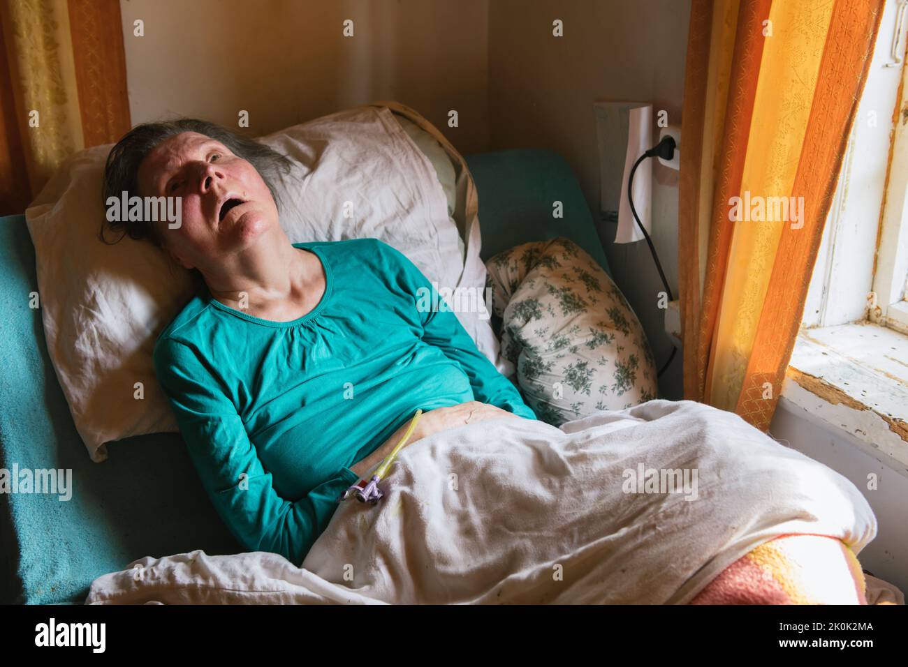 Senior woman with paralysis lying under blanket on medical bed near ...