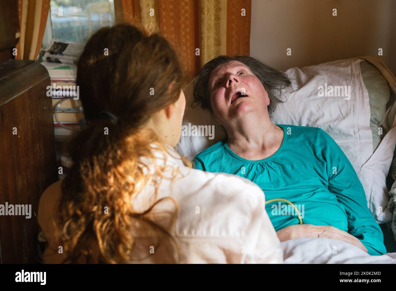 Back view of female nurse feeding paralyzed elderly lady with puree ...