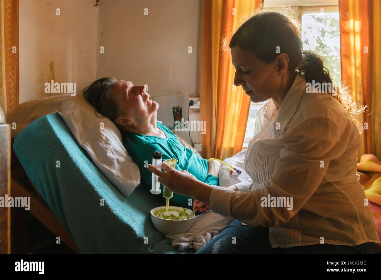 Side view of female nurse feeding paralyzed elderly lady with puree ...
