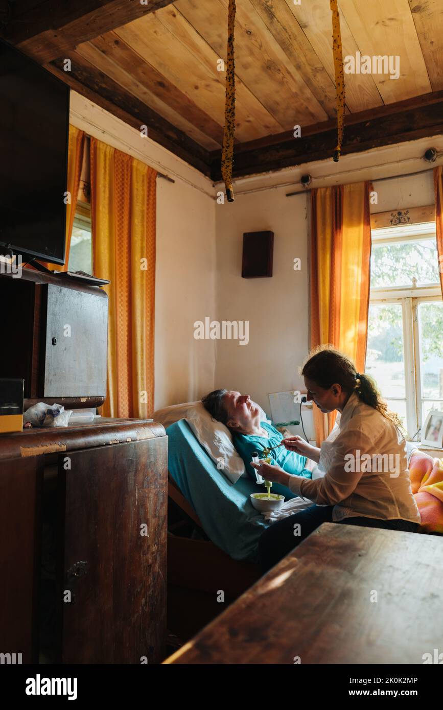 Side view of female nurse feeding paralyzed elderly lady with puree ...