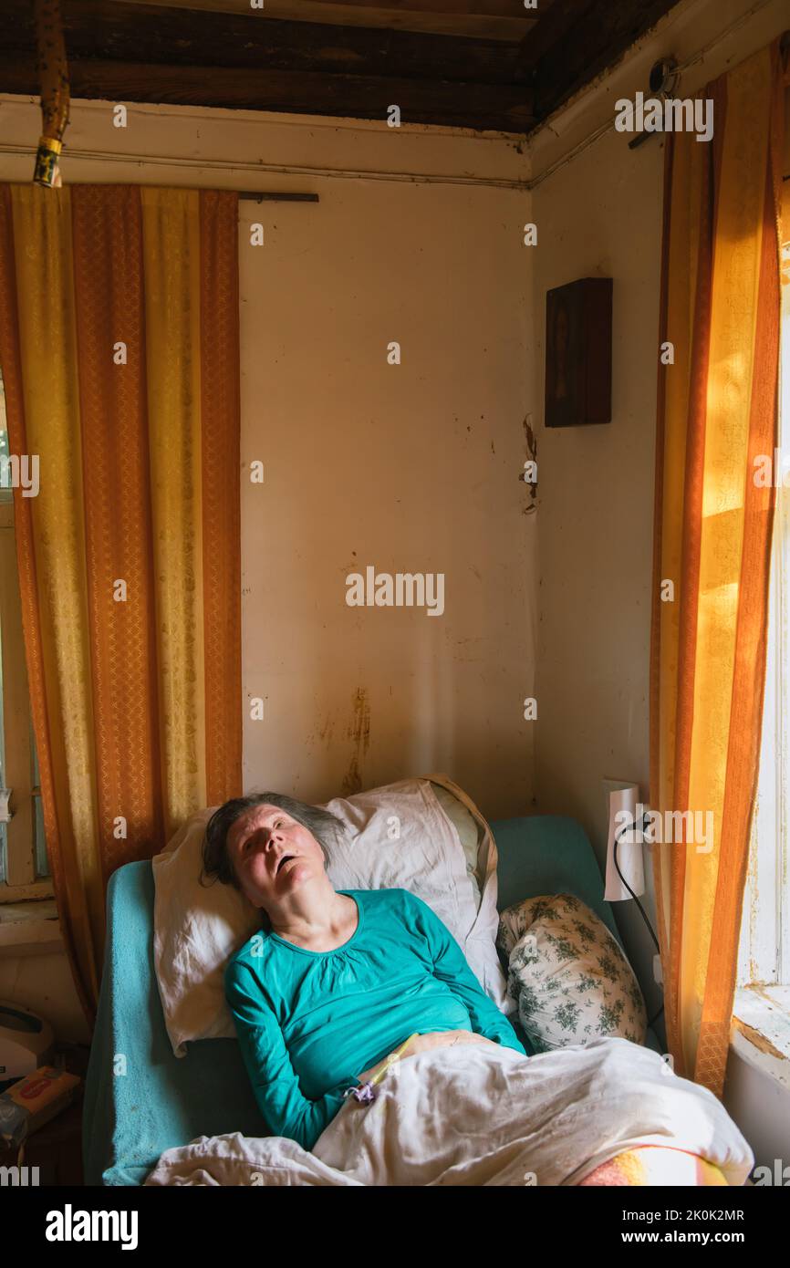 Senior woman with paralysis lying under blanket on medical bed near ...